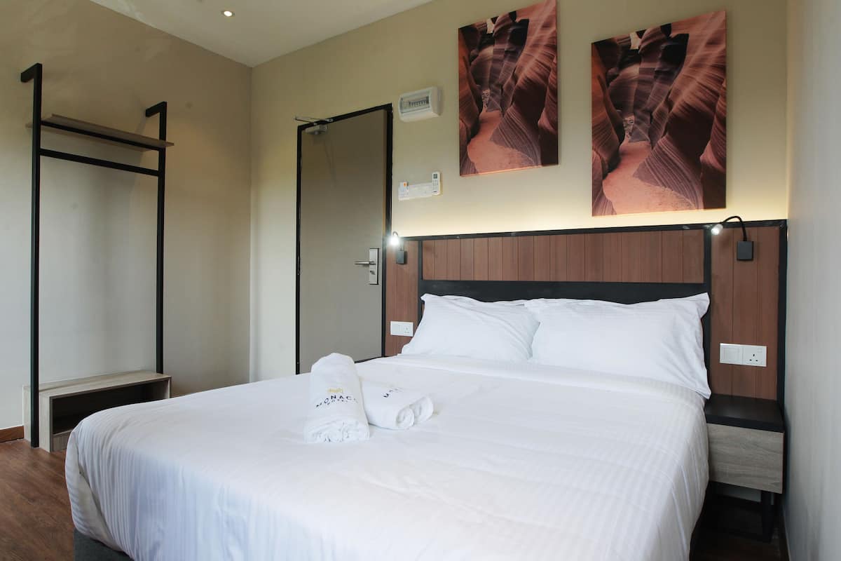 Quarto de hotel com cama, painel de cabeceira de madeira, televisão na parede e porta-toalhas.