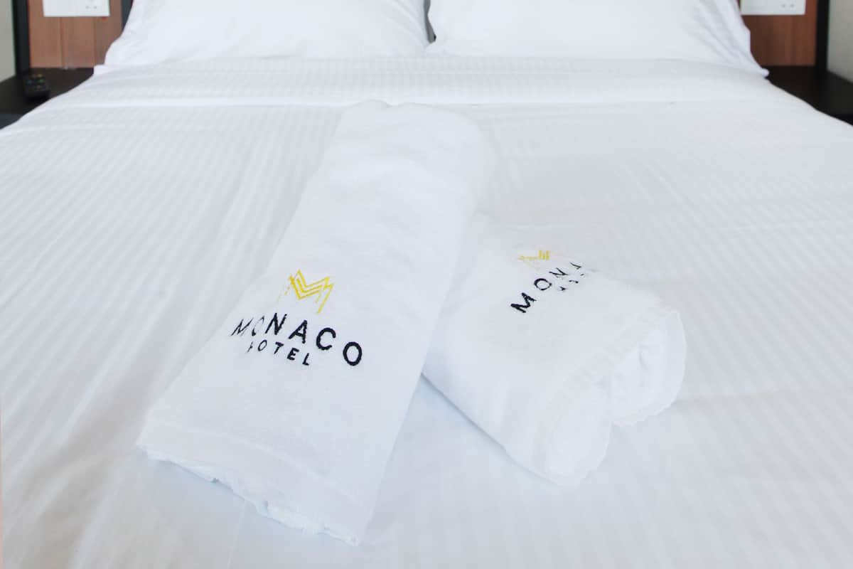 Quarto de hotel com cama, duas almofadas, cabeceira e duas luminárias fixadas na parede.