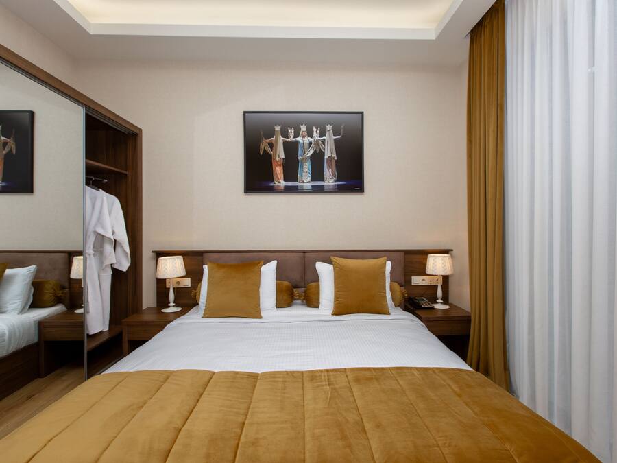 Quarto de hotel com uma cama grande, um espelho, um quadro na parede e uma janela com cortinas.
