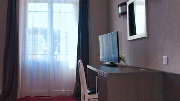 Quarto de hotel com escrivaninha, cadeira e uma janela grande com cortinas.