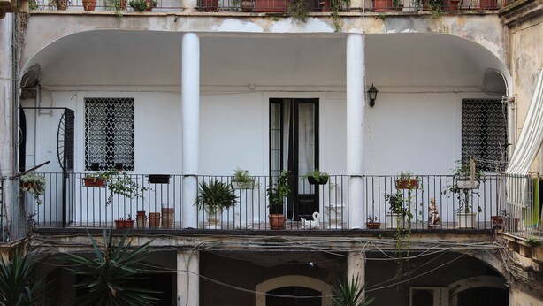Um edifício de vários andares com varandas, plantas em vasos e uma estátua.