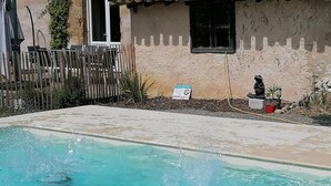 Piscina com água cristalina, rodeada por um muro de pedra e uma cerca de madeira.