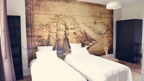 Quarto com duas camas, um mural de mapa grande na parede, guarda-roupa e luminária pendente.