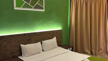 Quarto de hotel com cama, mesa de cabeceira, parede verde, decoração geométrica e cortina.