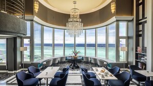 Um quarto espaçoso com uma grande janela curva que oferece vista para o oceano, um candelabro e amenidades de estar modernas.