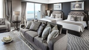 Quarto de hotel com uma cama grande, um sofá, uma mesa de centro e vista para o mar.