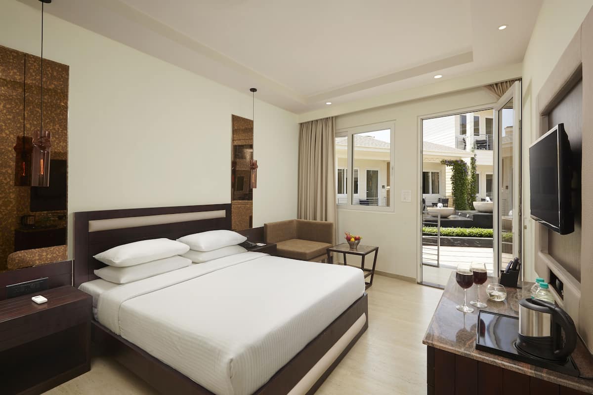 Quarto de hotel moderno com uma cama grande, área de estar, televisão e vista para a varanda.