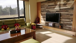 Uma sala de estar moderna com um sofá verde, uma mesa de centro de madeira e uma TV de tela plana fixada numa parede de madeira.