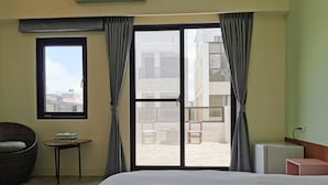 Quarto de hotel com cama grande, uma cadeira, uma mesa pequena e vista para a varanda externa.