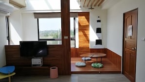 Quarto moderno com televisão, detalhes em madeira, uma mesinha e vista para o exterior.