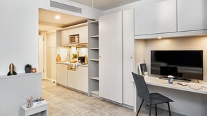 Cozinha moderna com eletrodomésticos embutidos, área de refeições com uma cadeira e uma TV em um console branco.