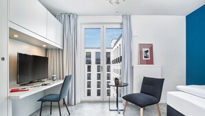Quarto moderno com televisão de tela plana, duas cadeiras, uma mesinha e uma cama.