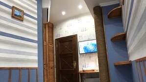 Um corredor com paredes listradas, uma porta de madeira, uma televisão e uma maquete de navio.
