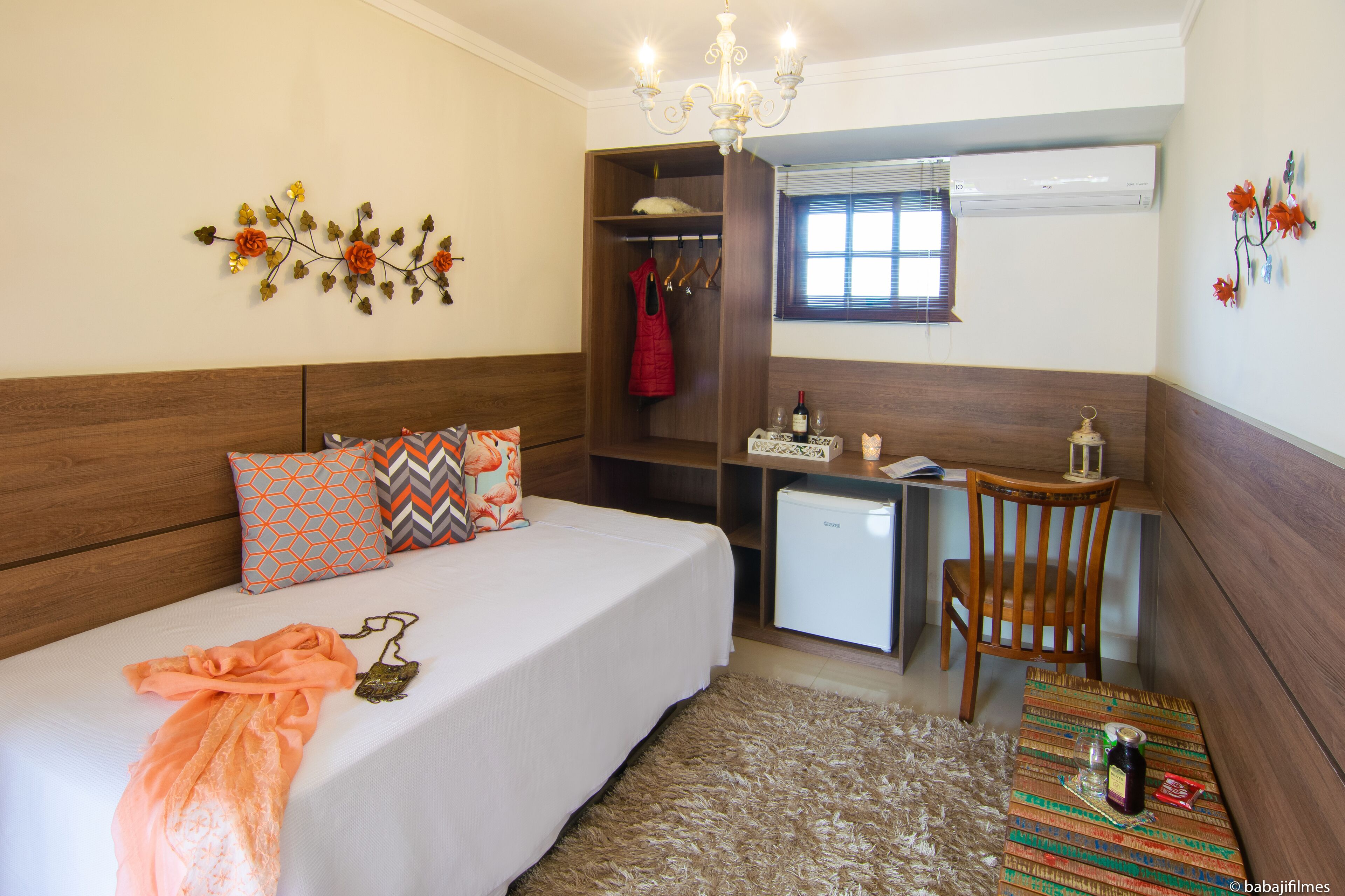 Quarto com cama, escrivaninha, cadeira, guarda-roupa e um pequeno frigorífico.