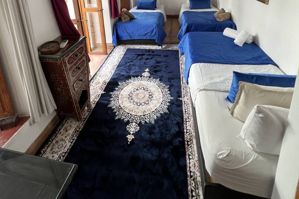 Quarto de hotel com duas camas, um tapete grande e ornamentado e um espelho na parede.