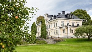 Um edifício grande e histórico com fachada simétrica, janelas amplas e um gramado bem cuidado.