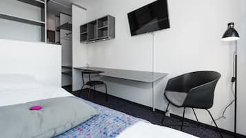 Quarto de hotel com cama, escrivaninha, cadeira, televisão e abajur.