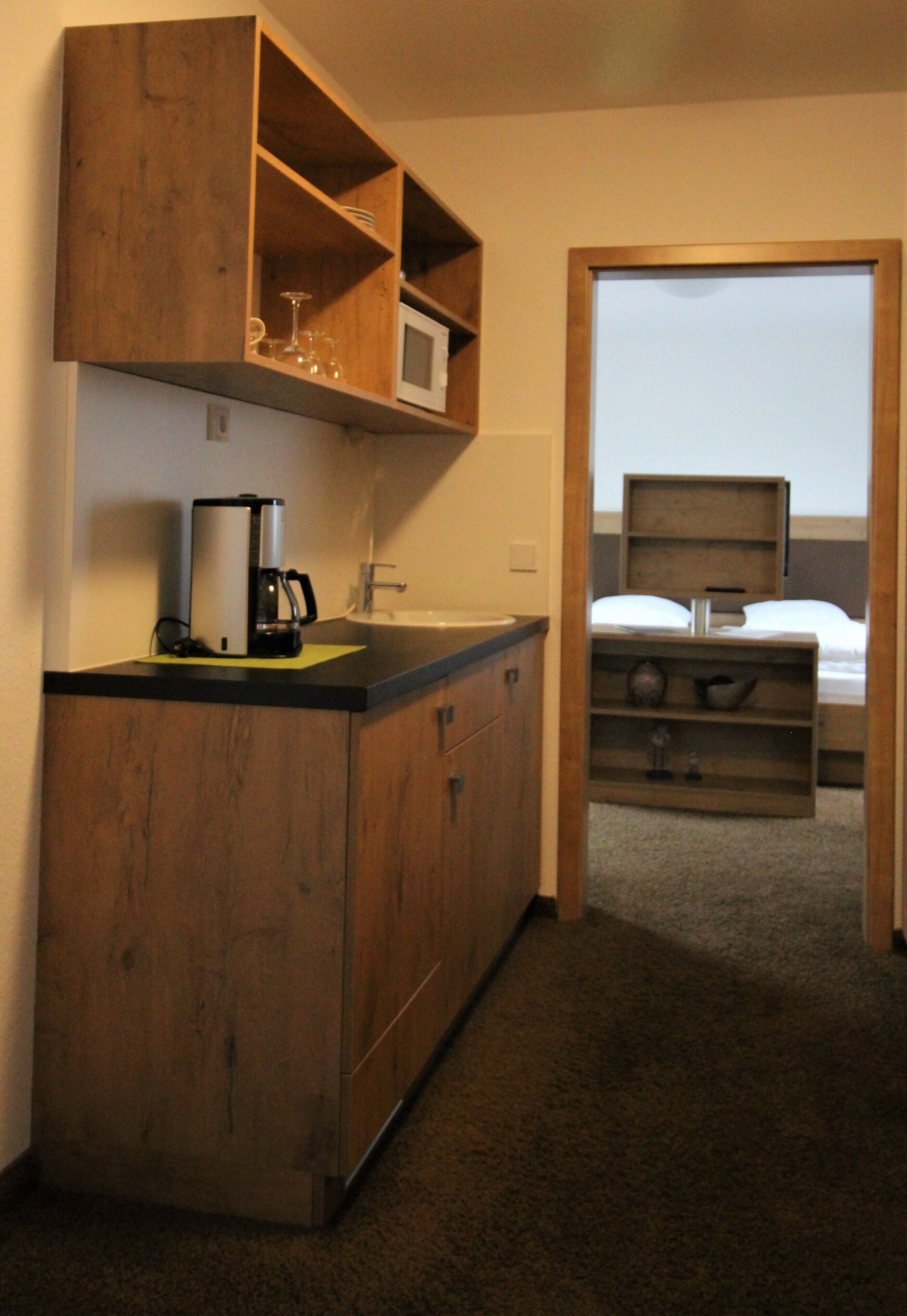 Quarto de hotel pequeno com cozinha compacta, uma cama e guarda-roupa de madeira.