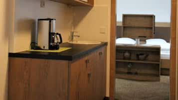 Quarto de hotel pequeno com cozinha compacta, uma cama e guarda-roupa de madeira.
