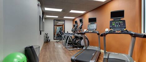 Uma academia com esteiras, bolas de exercício e um espelho.