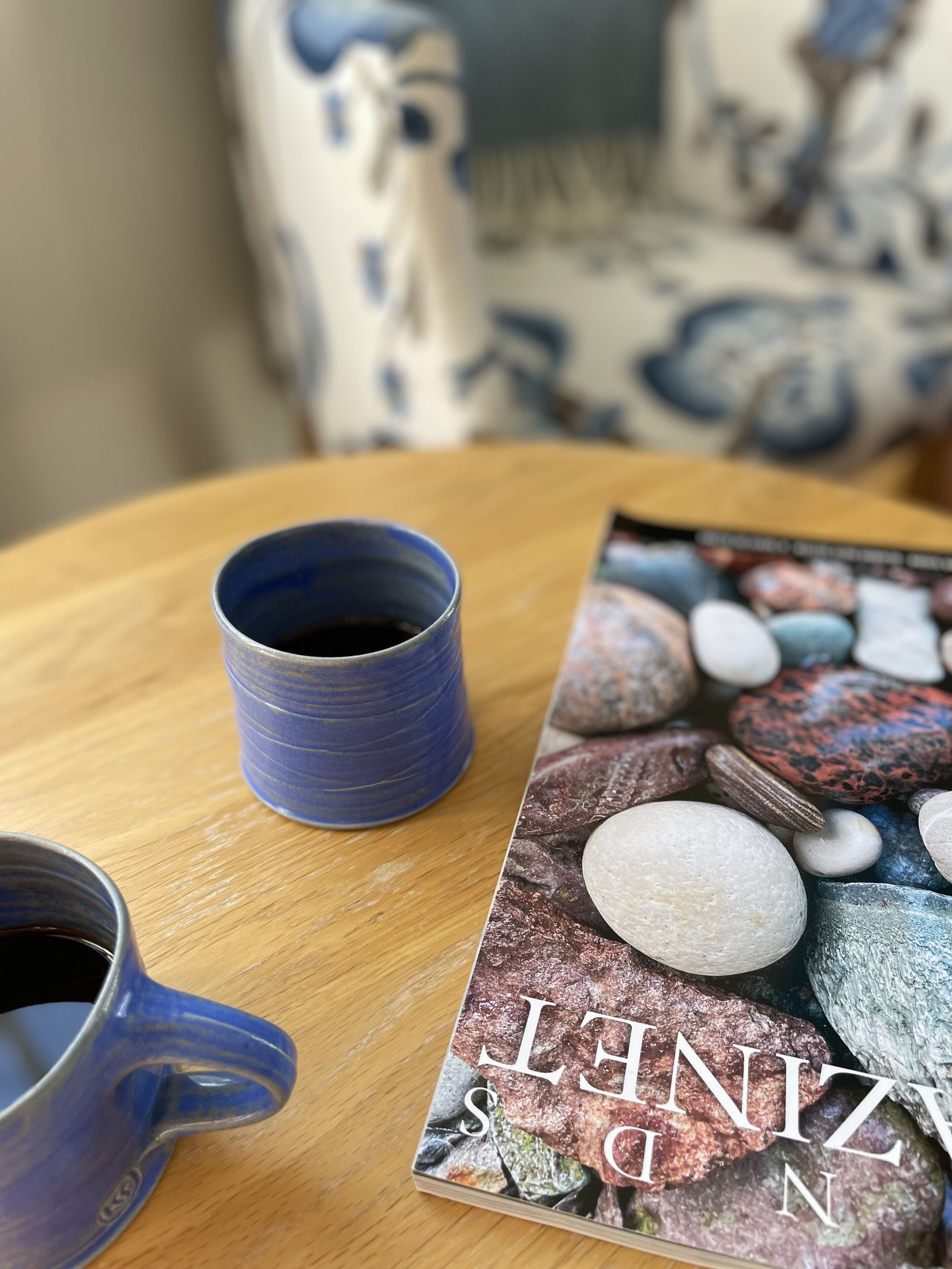 Uma mesa de madeira com duas canecas de cerâmica, uma com café e outra vazia, e um livro intitulado 