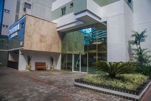 Um edifício moderno com entrada de vidro, um banco de madeira e plantas em vasos.