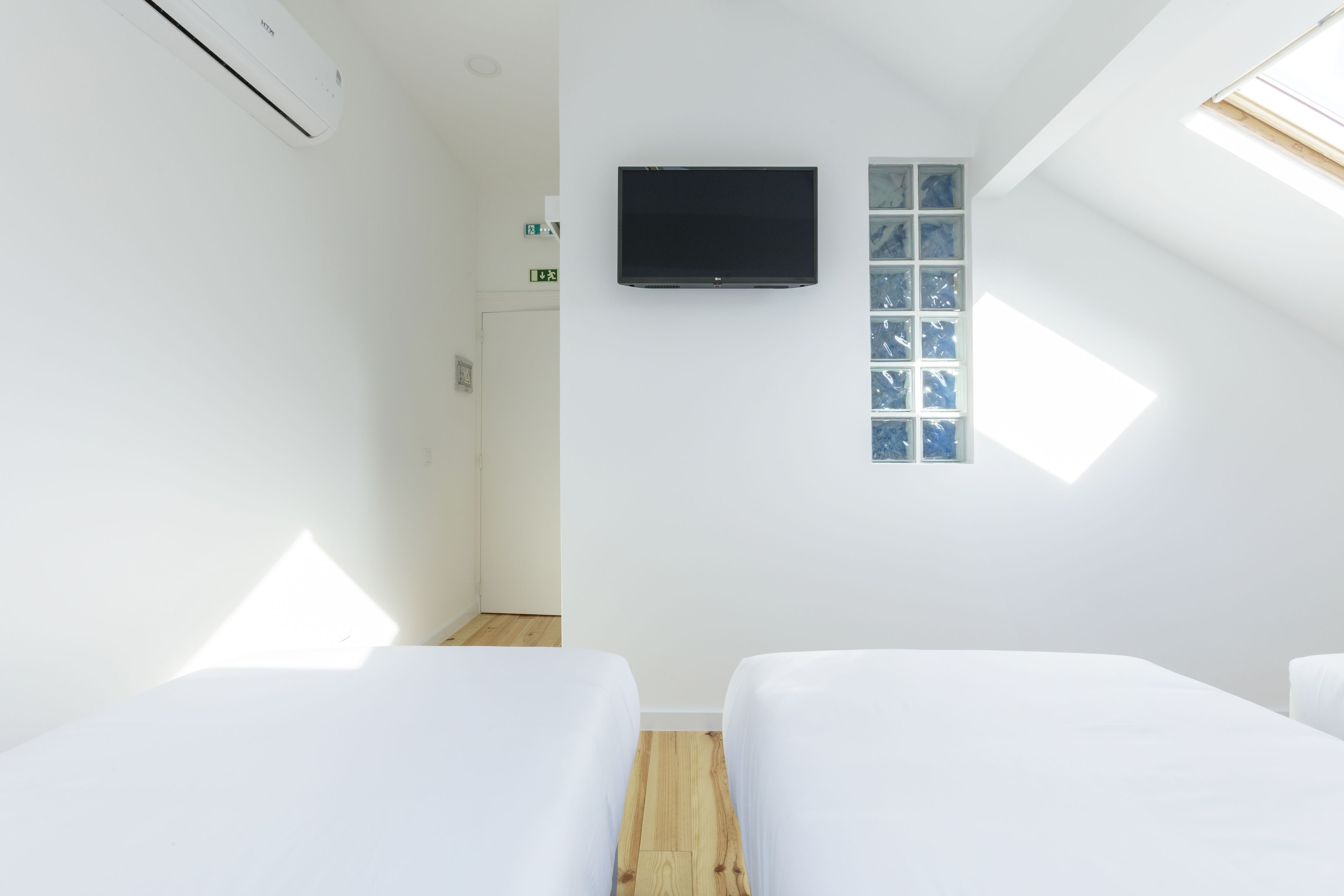 Quarto moderno e bem iluminado, com duas camas, televisão de tela plana na parede e um claraboia que permite entrada de luz natural.