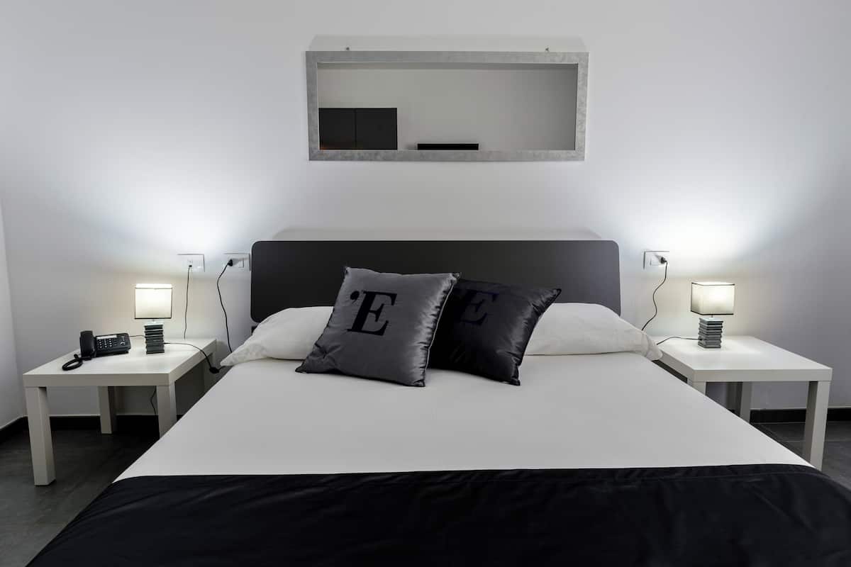 Quarto de hotel com cama, duas mesas de cabeceira, um criado-mudo, abajur, telefone e espelho.