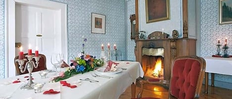 Uma sala de jantar com lareira, mesa posta para refeição e uma cadeira estofada vermelha.