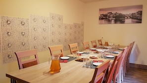 Uma sala de jantar com uma mesa comprida posta para refeição, cadeiras e uma grande obra de arte na parede acima da mesa.