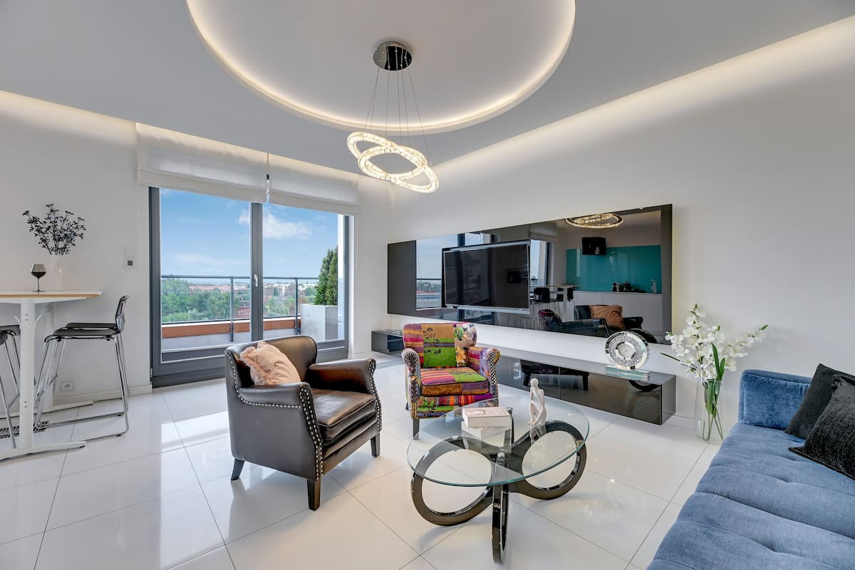 Uma sala de estar moderna com uma televisão grande, um sofá, uma poltrona colorida e uma mesa de centro de vidro.