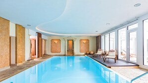 Uma grande piscina interior com paredes de vidro transparente, chão de pedra e vista para o exterior.