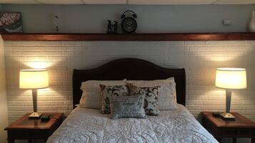 Cama bem arrumada com colcha branca, duas luminárias de cabeceira e almofadas decorativas.