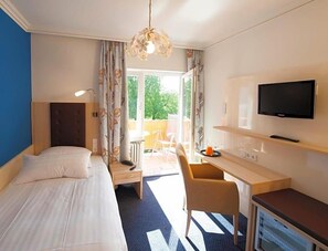 Quarto de hotel com cama, escrivaninha, cadeira, televisão e vista para o exterior.