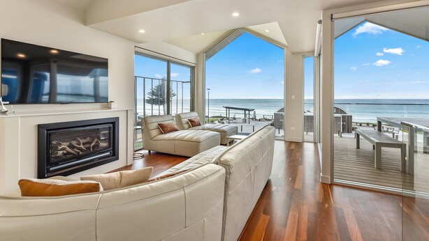 Uma sala de estar moderna com um sofá grande, uma lareira e vista para a praia.