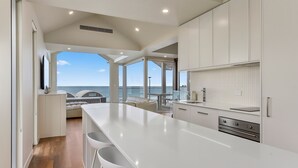 Cozinha moderna com uma ilha grande, armários brancos e vista para o oceano.