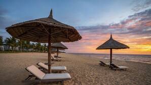 Uma praia com guarda-sóis de palha e espreguiçadeiras.
