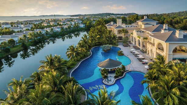 Um resort com uma piscina grande, palmeiras e vista para o mar.