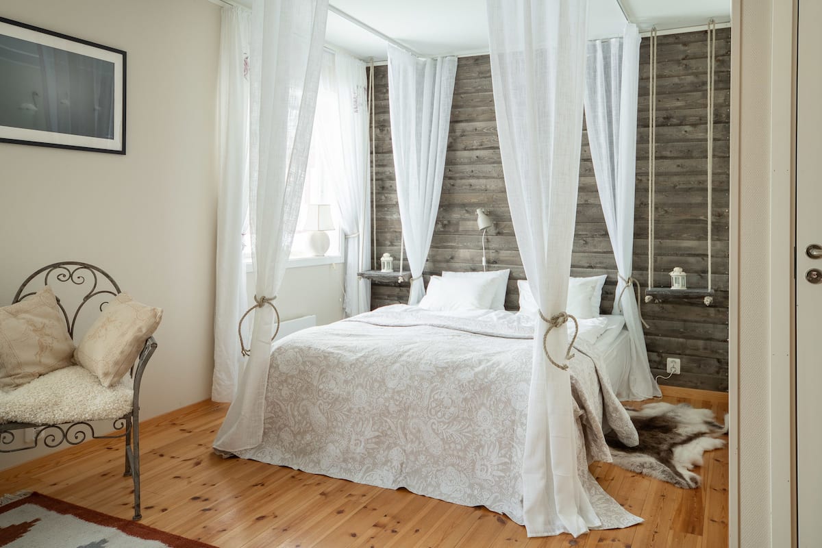 Quarto com cama de dossel, piso de madeira e colcha branca.