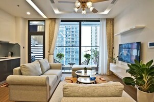 Uma sala de estar moderna com sofá, mesa de centro e televisão. Há uma varanda com plantas e vista para a cidade.