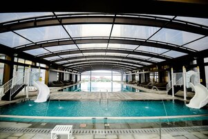 Piscina interna com duas escorregas, teto de vidro e vista para o exterior.