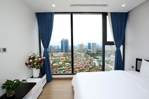 Quarto moderno com uma cama grande, vista para o horizonte urbano e um vaso de planta.
