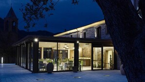 Um edifício moderno com fachada de vidro, revestimento de pedra e área de refeições com mesas e cadeiras.