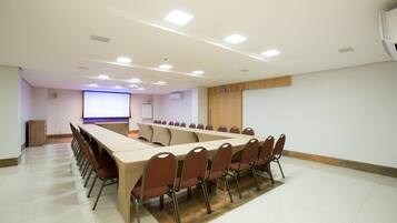 Uma sala de conferência com uma mesa comprida, cadeiras, uma tela de projetor e um quadro branco.