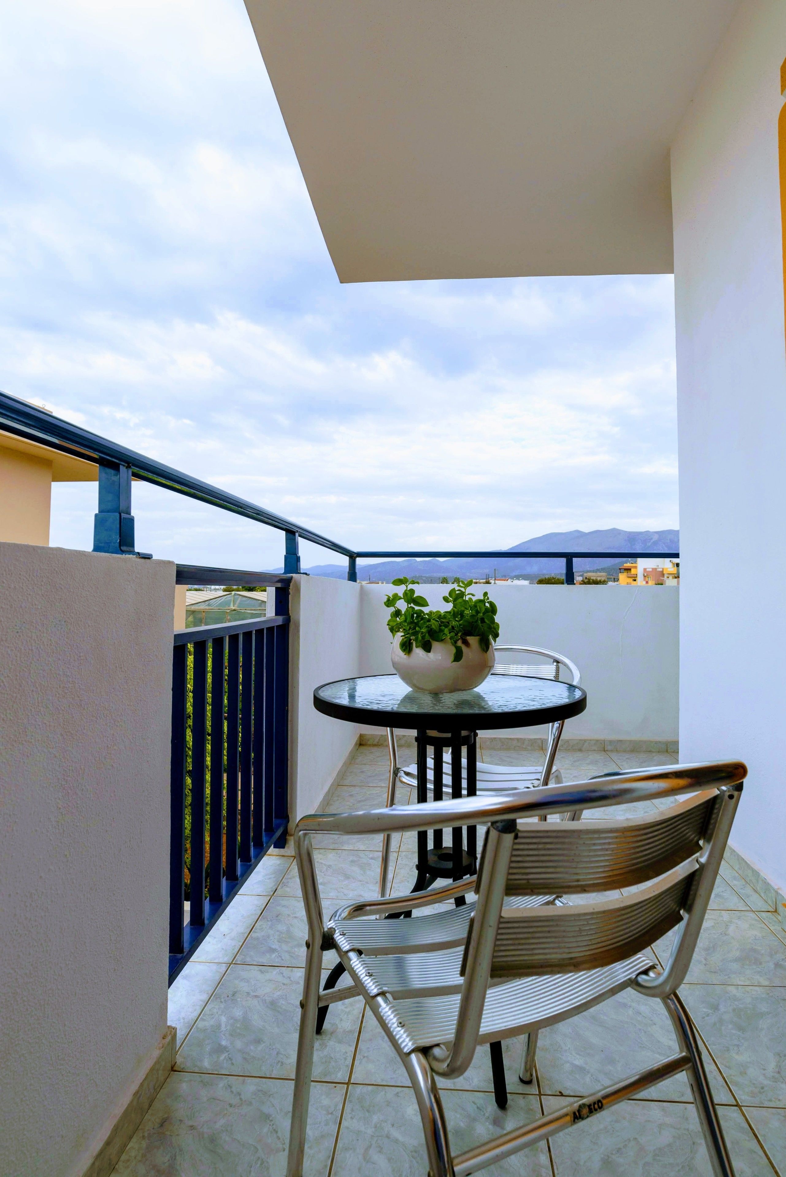 Uma varanda com mesa e cadeiras, um vaso de planta e vista para montanhas ao longe.