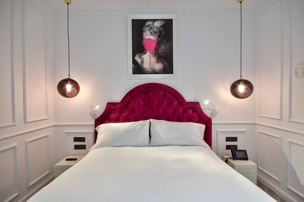 Quarto com cabeceira estofada vermelha, roupa de cama branca e iluminação pendente.