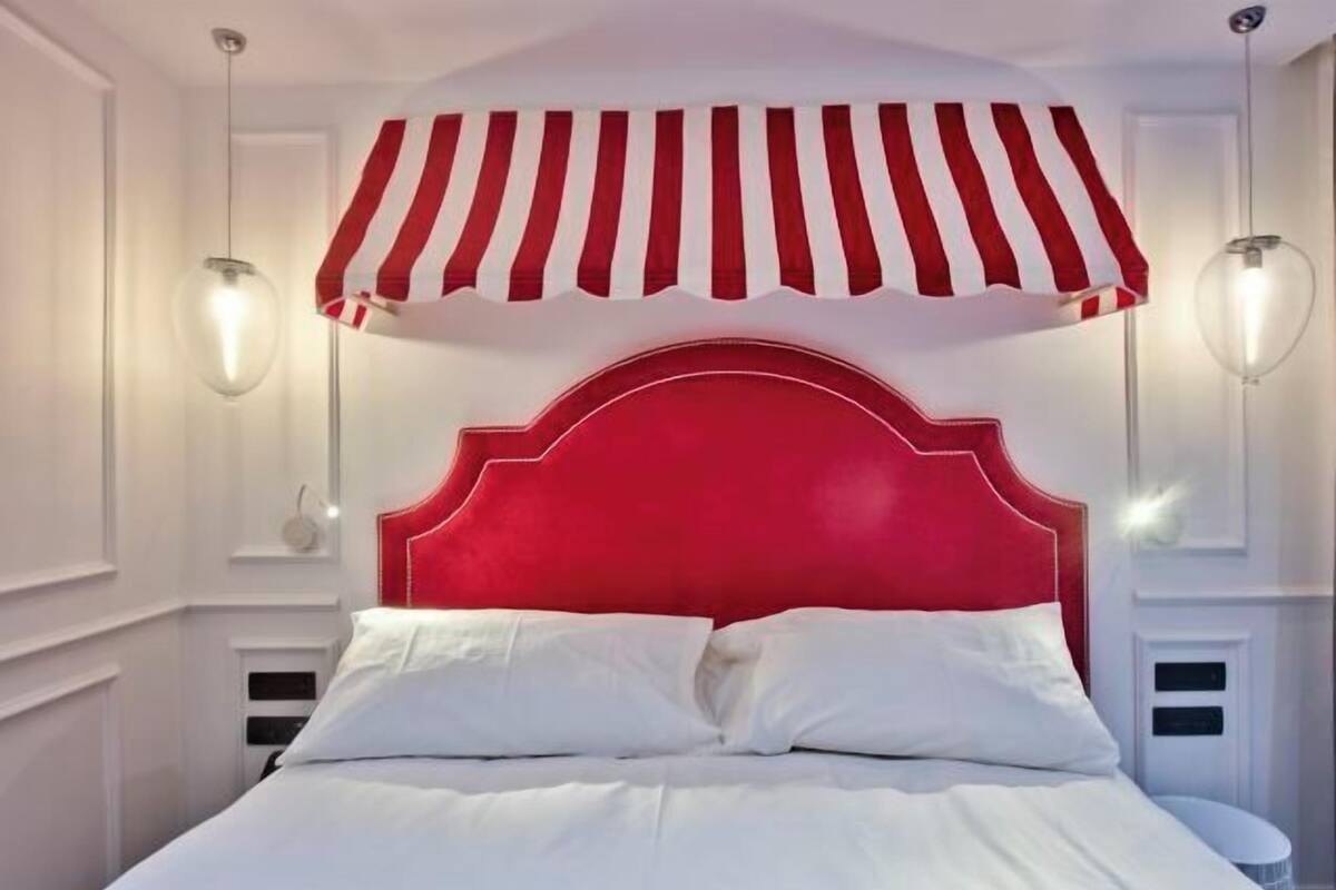 Uma cama com cabeceira vermelha, roupa de cama branca e um dossel listrado.