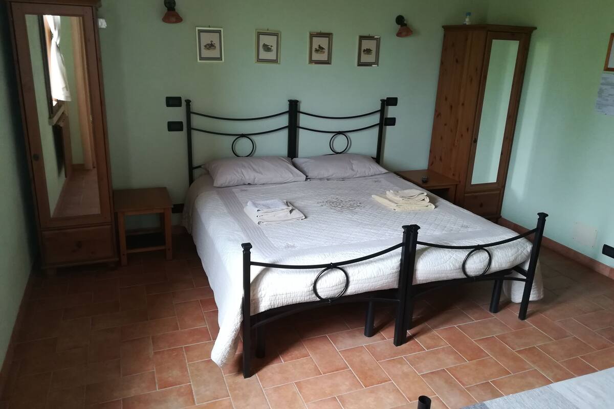 Quarto com cama, guarda-roupa de madeira, espelho e pequena mesa.