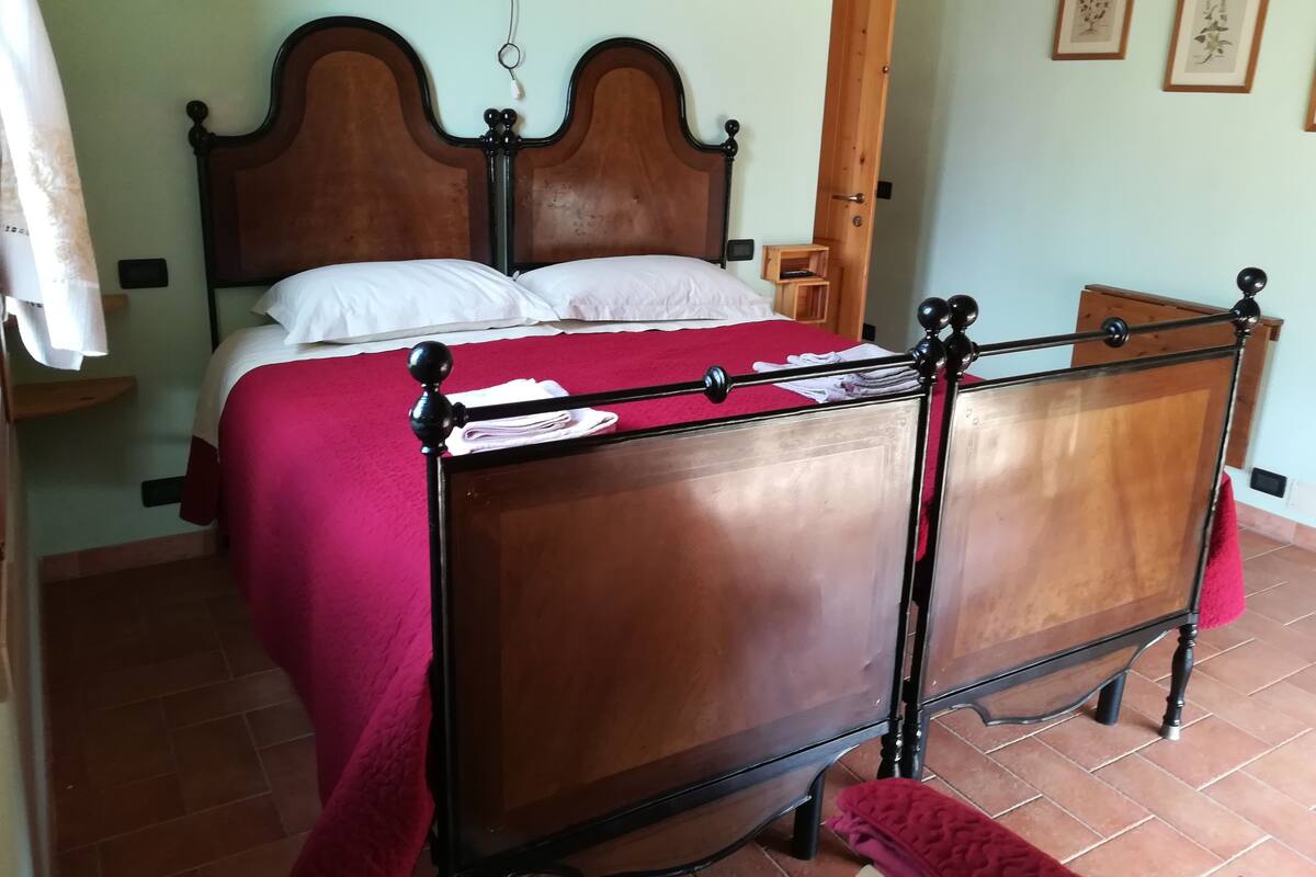 Uma cama de madeira com estrutura de metal, roupa de cama branca e um cobertor vermelho.