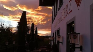 Área externa com mesas e guarda-sóis, um edifício com um letreiro em formato de coração, e um céu ao entardecer.
